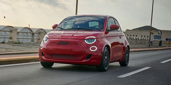 Side view of a 2024 Fiat 500e being driven in a city at night.
