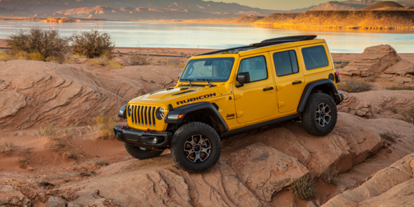 Yellow 2020 Jeep Wrangler driving through rocky terrain at sunset